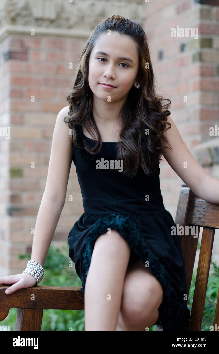 An eleven year old mixed race girl (Asian/Caucasian) sits on a bench ...