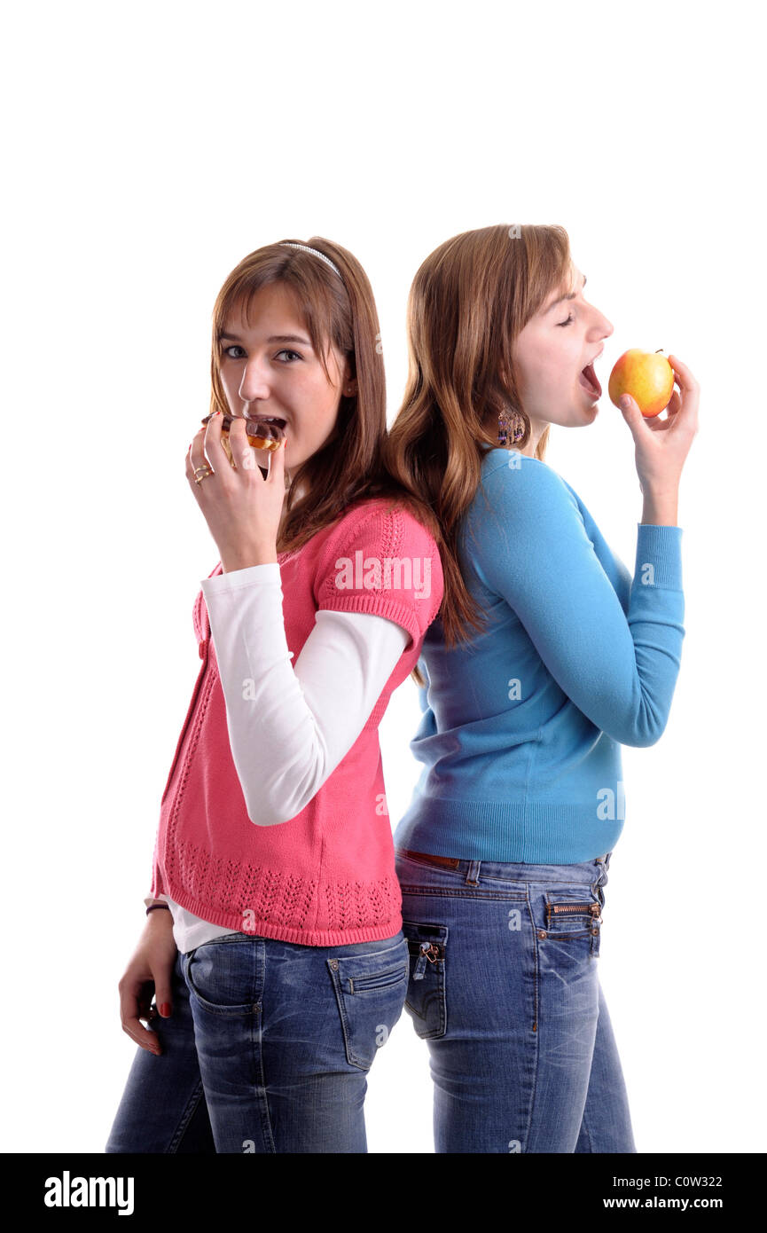 two young women stading back against back , one eating an apple, one ...