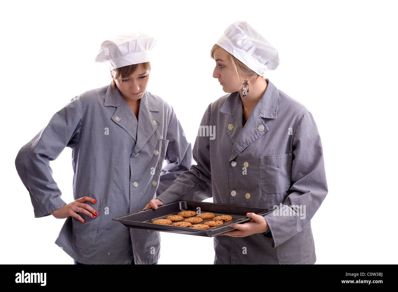 two young cooks in cook clothes inspecting cookies on a plate. isolated ...