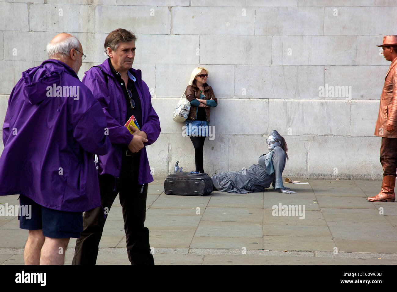 Two men wait whilst street performers rest and talk in the background ...