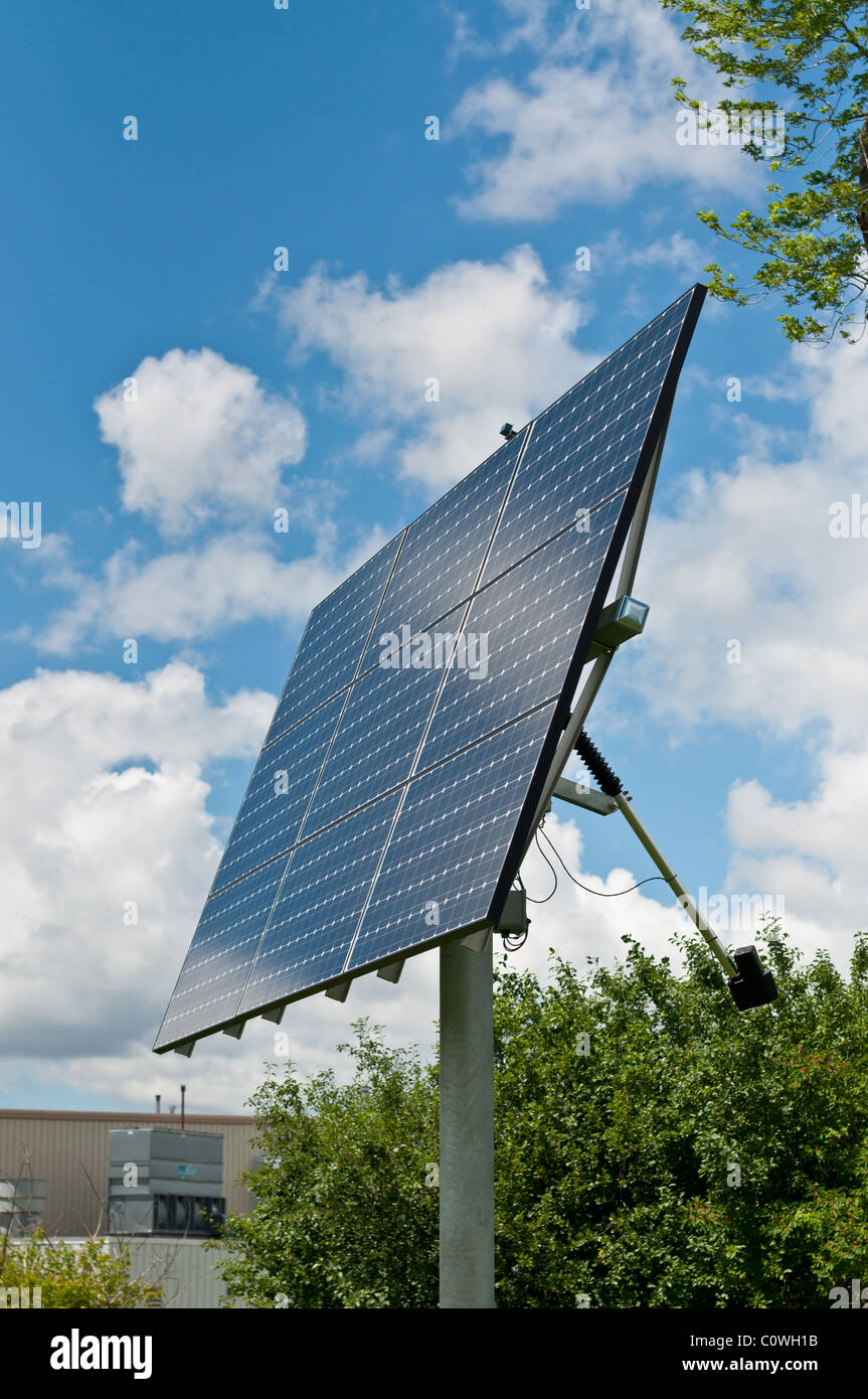 A photovoltaic solar panel array with a blue sky and green leaves in ...