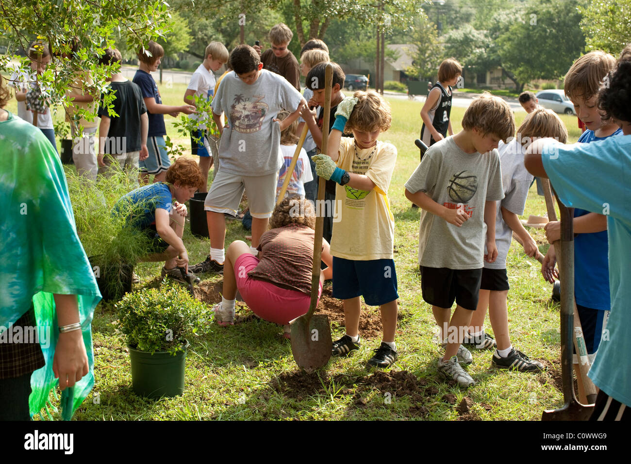 Fifth-grade students dig holes for plants on elementary school grounds ...