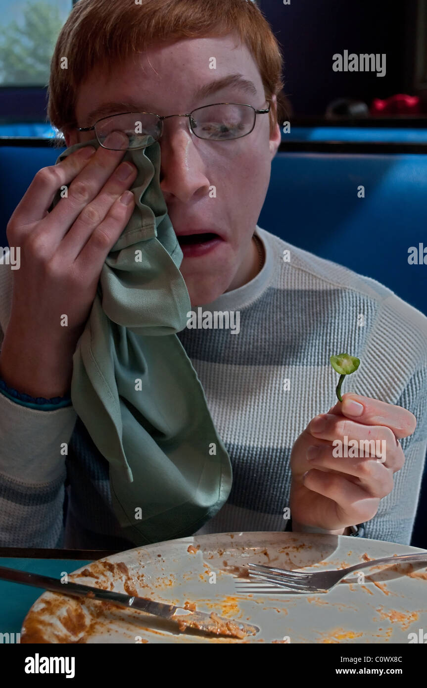 A teenager wipes his teary eye after eating a serrano pepper Stock ...