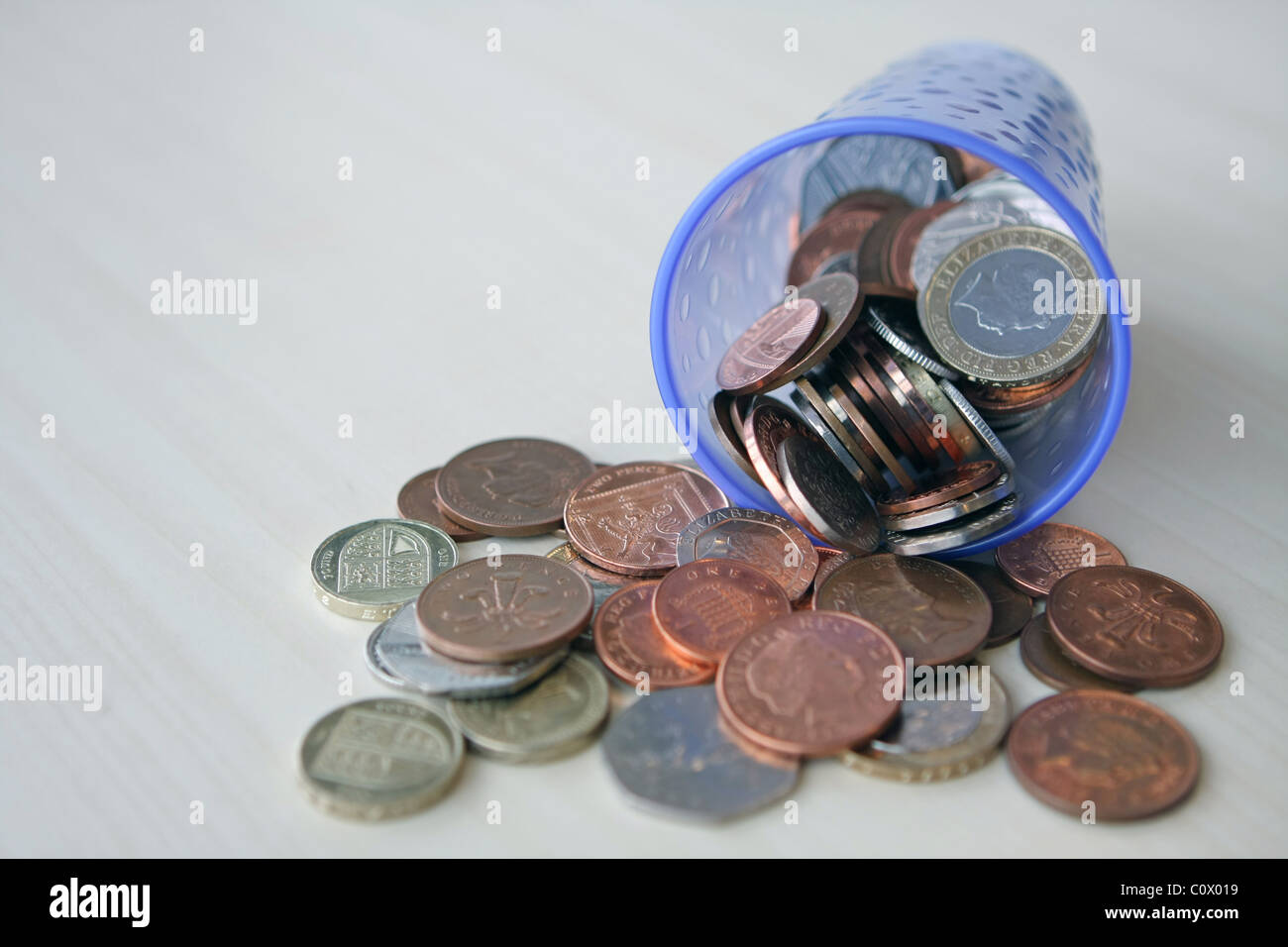Sterling coins spilling out of an upturned plastic cup Stock Photo - Alamy
