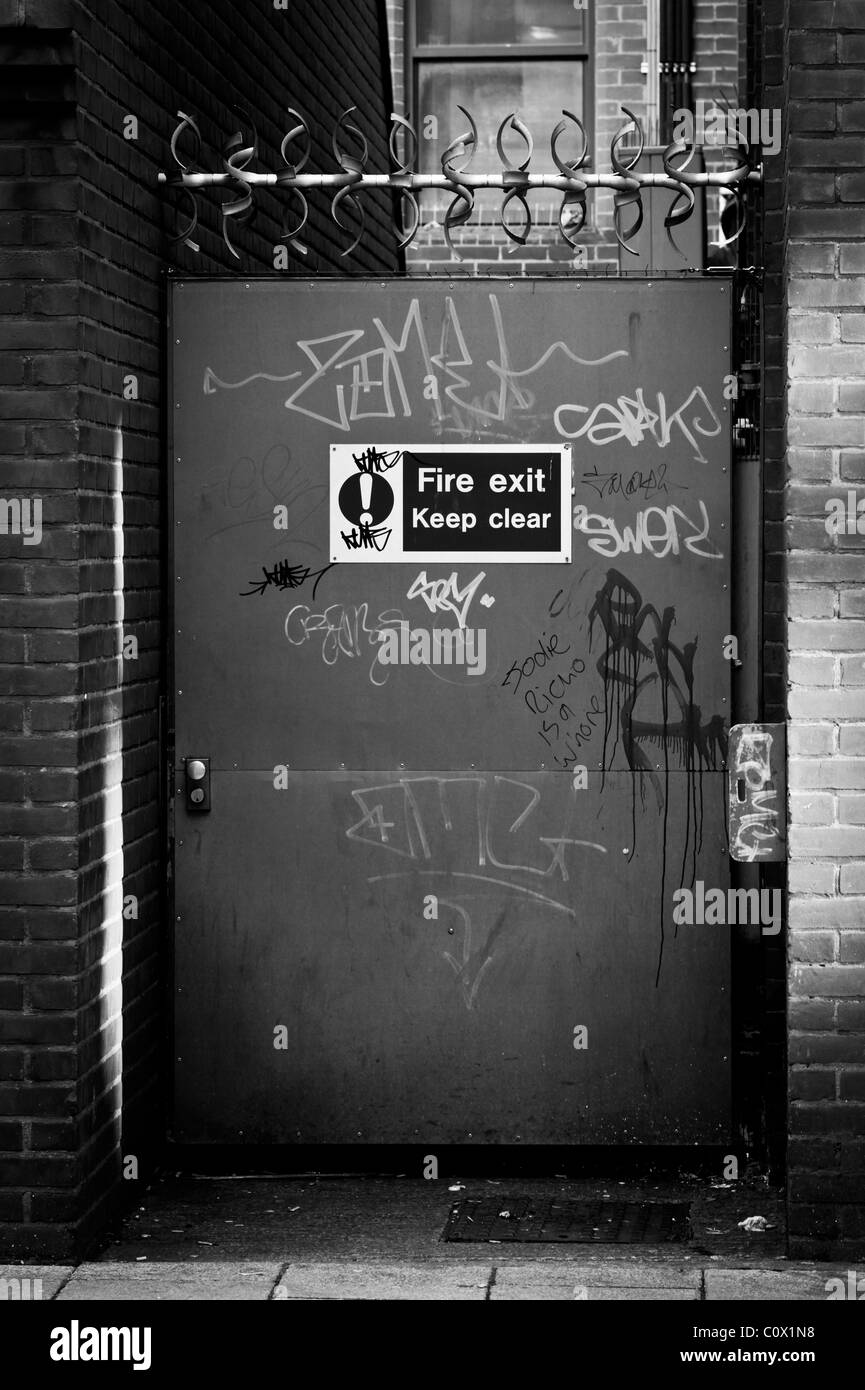 A vandalised urban fire exit doorway with graffiti and security spikes ...