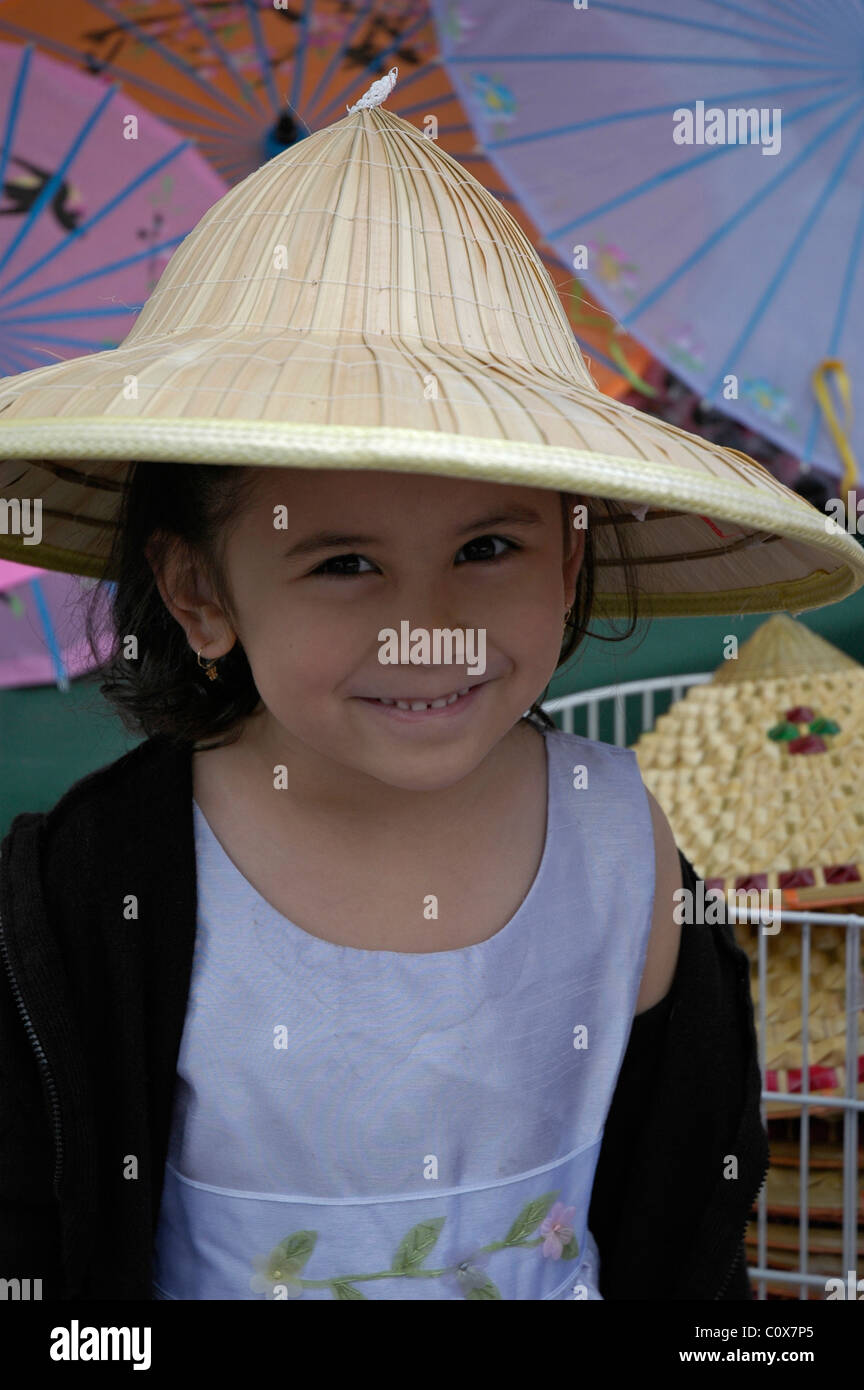 A cute young Asian/Caucasian girl wears a reed hat at an Asian Festival ...