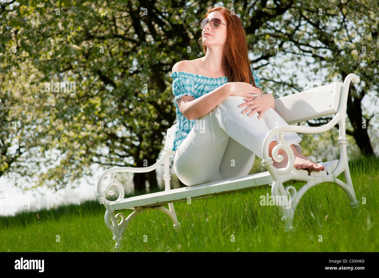 Red hair woman sunbathing on white bench in a meadow; shallow DOF Stock ...