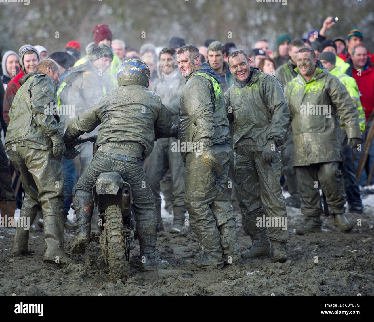 Man on muddy motocross scrambling motorcycle with team of dirty helpers ...