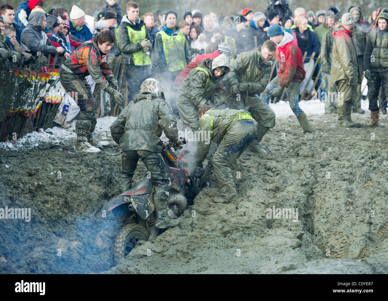 Man on muddy motocross scrambling motorcycle pulled by rope and team of ...