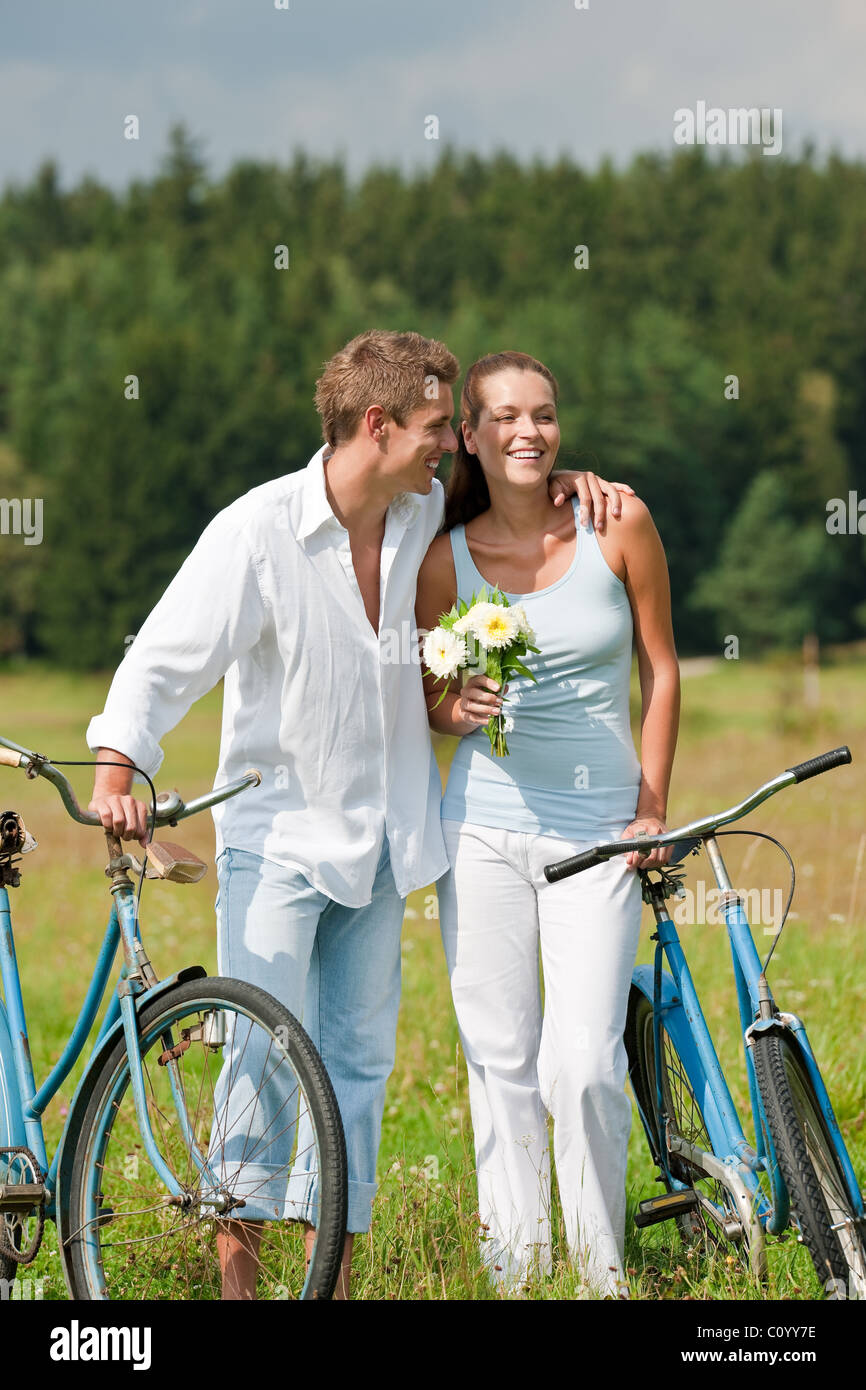 Romantic young couple walking with old bike in meadow on sunny day ...