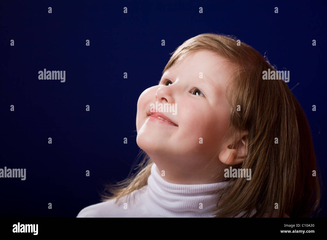 Happy Child looking up with interest over dark blue background Stock ...