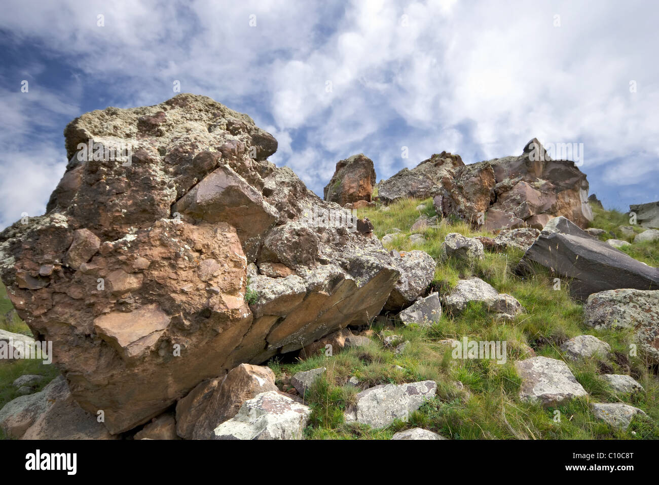 Heap of rocks, boulders and stones in grass against a blue sky with ...