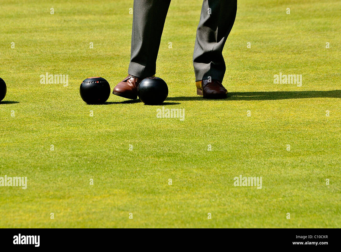 A pair of legs standing over some bowling balls, there is one pair of ...