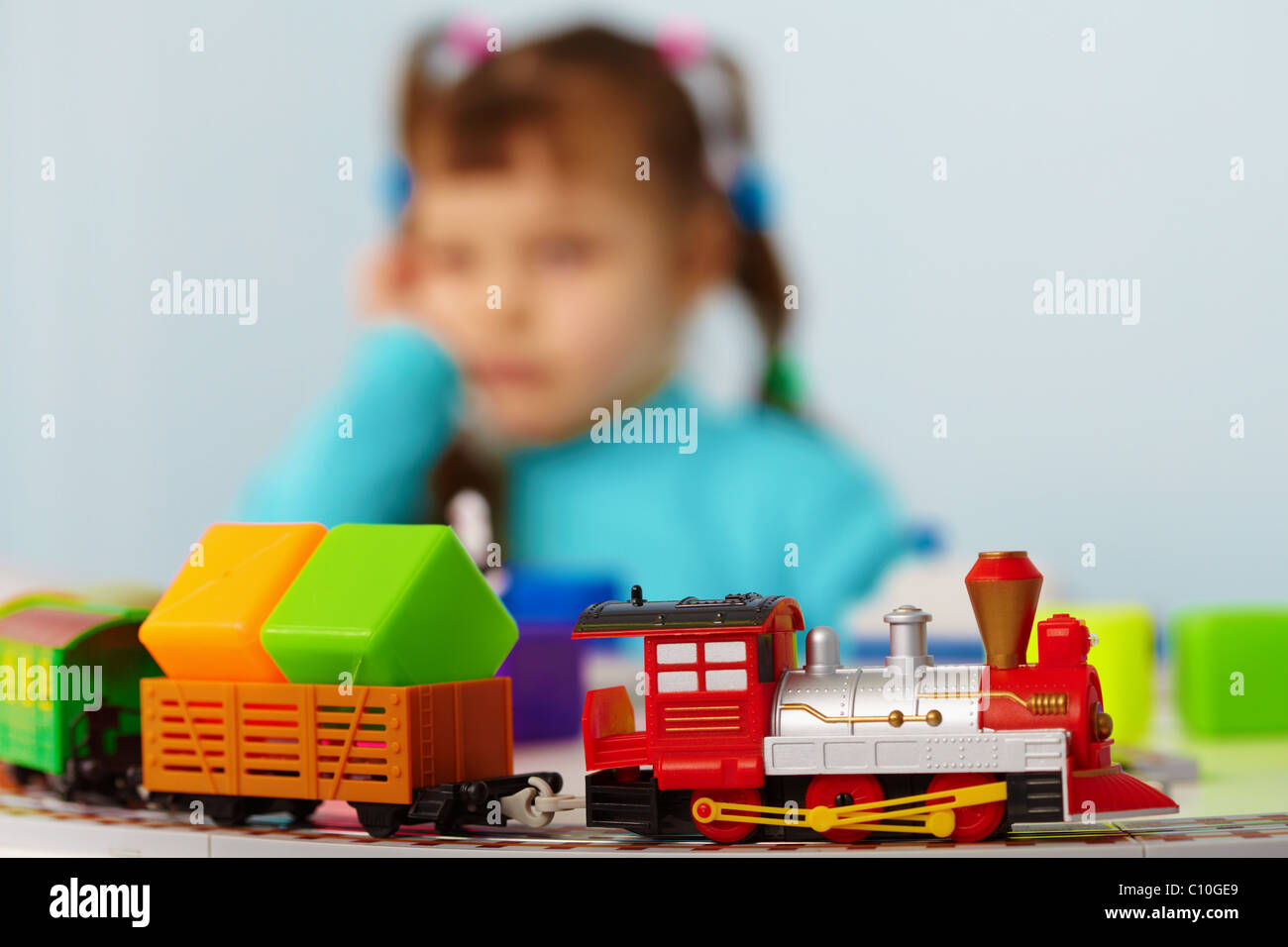 Little girl bored playing with toys alone on blue background Stock ...