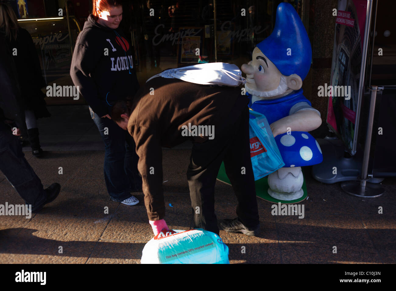 A gnome cartoon character appears to be sniffing the behind of a passer ...
