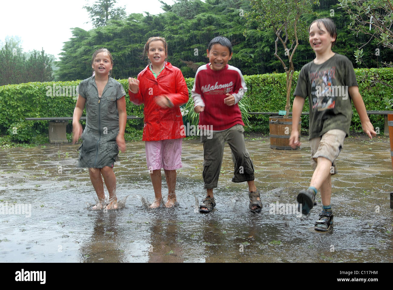 Four children jumping in rain and puddle Stock Photo - Alamy