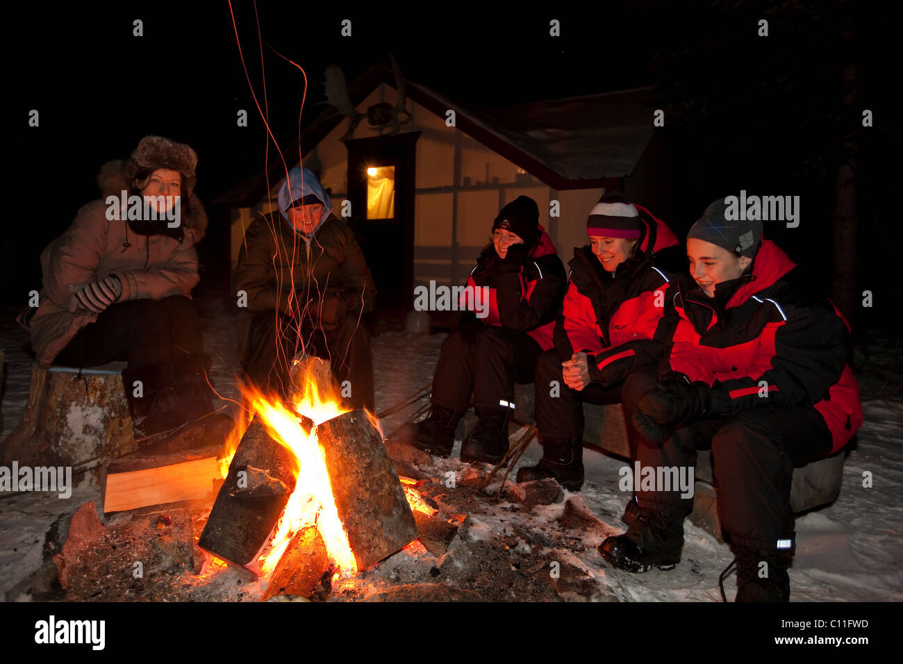 People sitting at a camp fire, illuminated wall tent, cabin behind ...