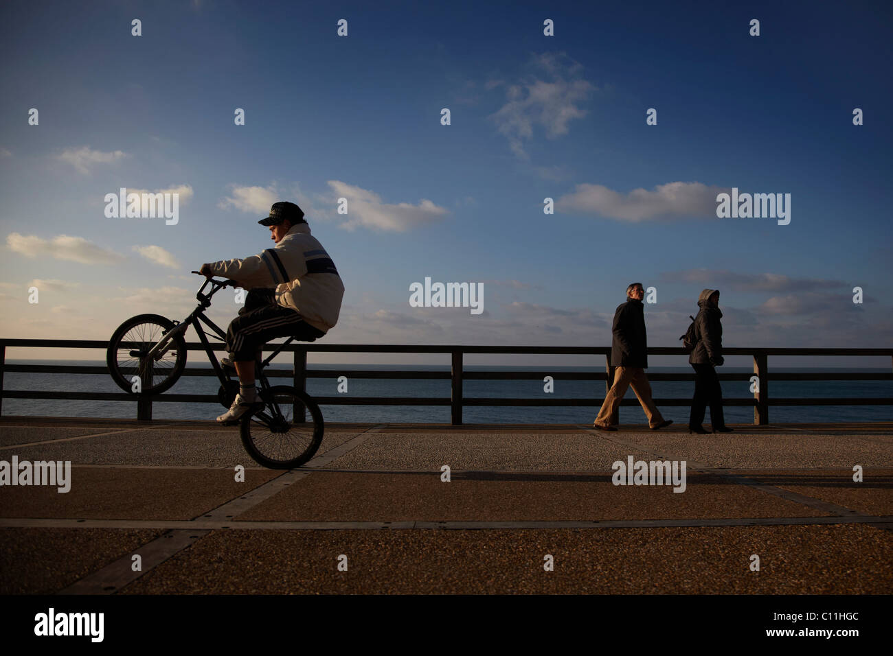 An elderly couple walking along a beach promenade, while a boy performs ...