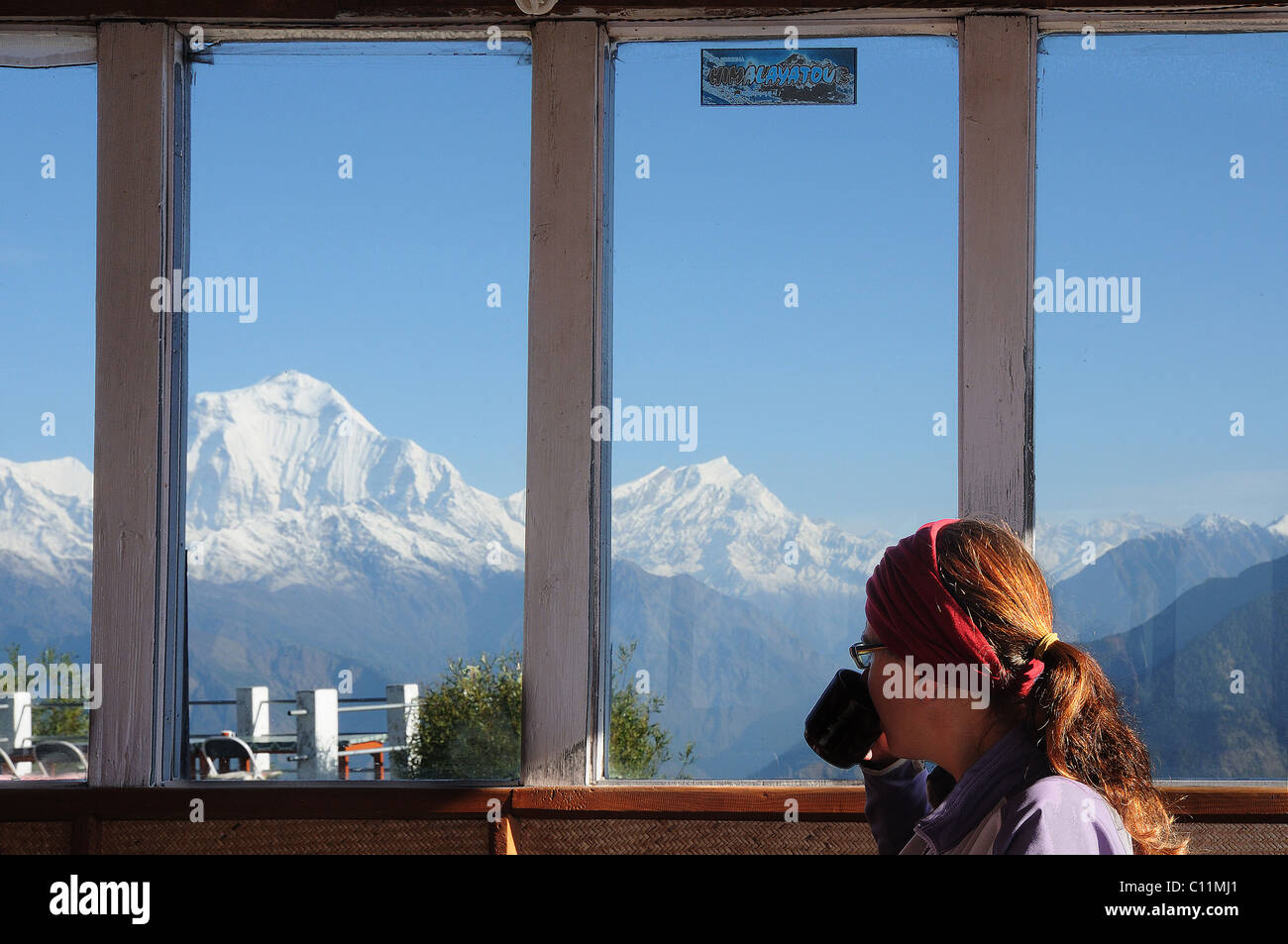 A trekker drinking tea in a lodge and looking at the mountains through ...