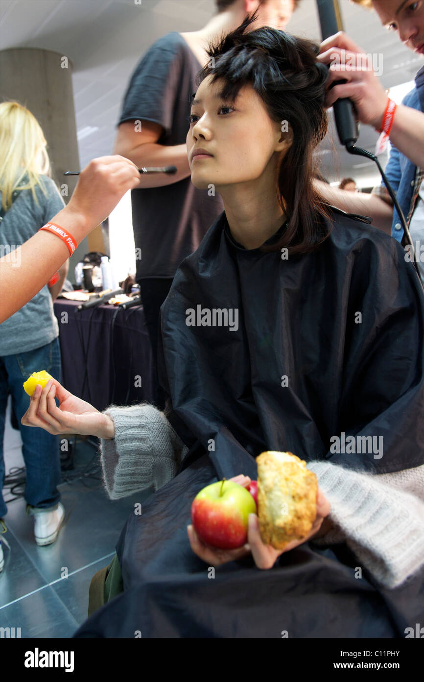 Clutching a healthy snack, a model is styled backstage at the Jonathan ...