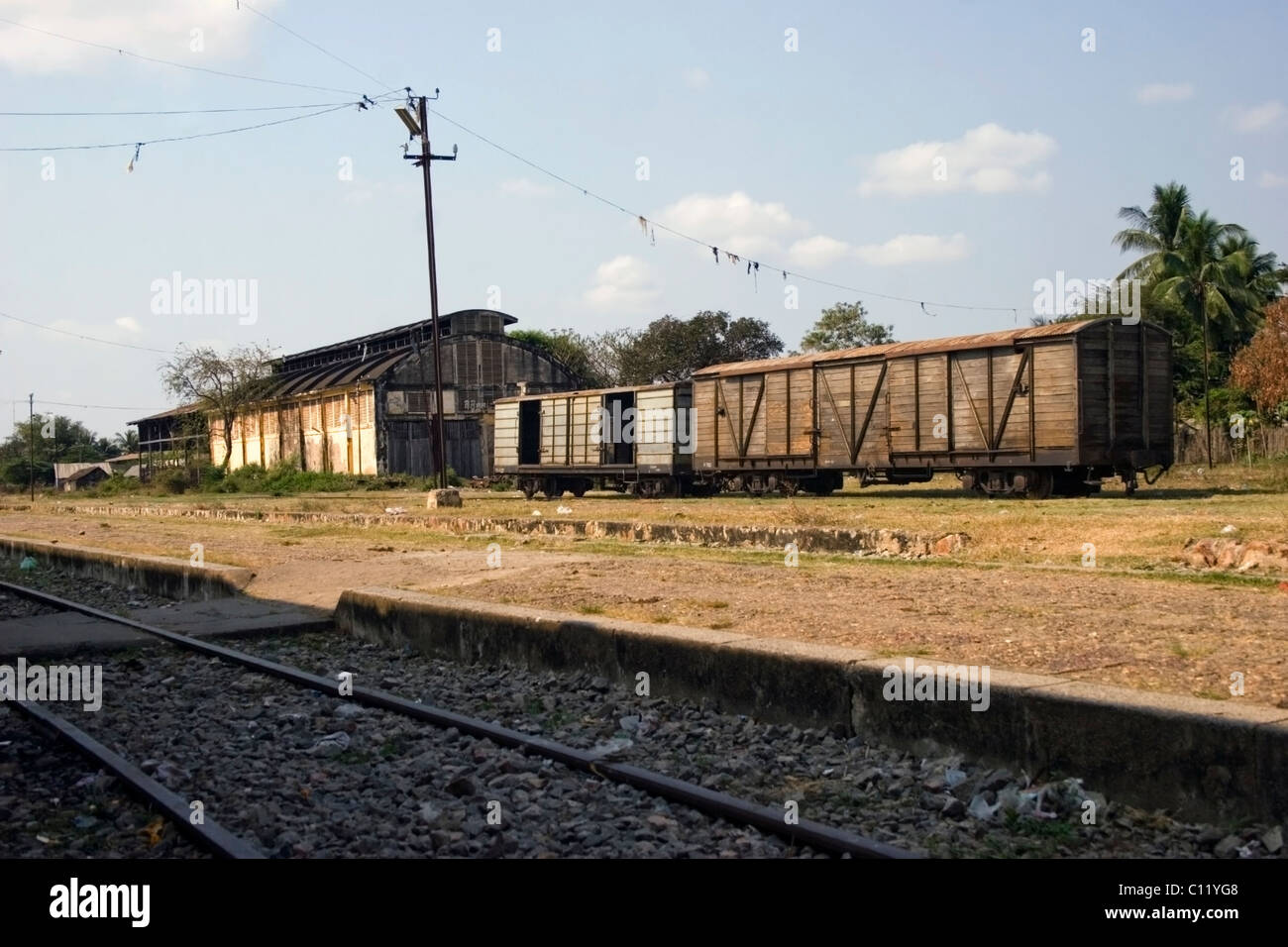 Wooden train boxcars are sitting on tracks near a dilapidated building ...
