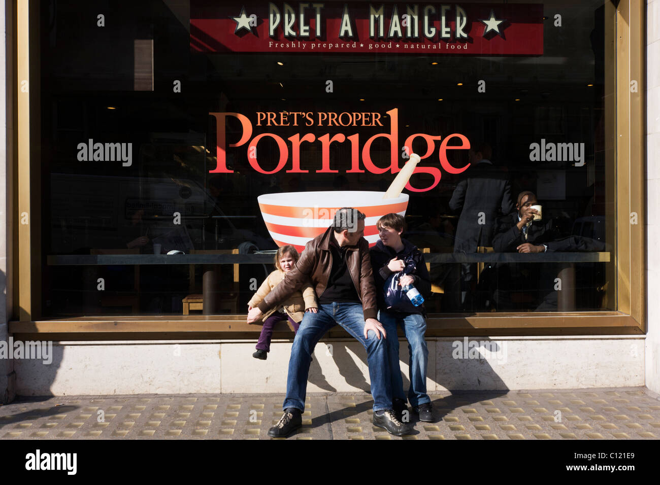 A father with his two children sits on a ledge outside a Pret a Manger ...