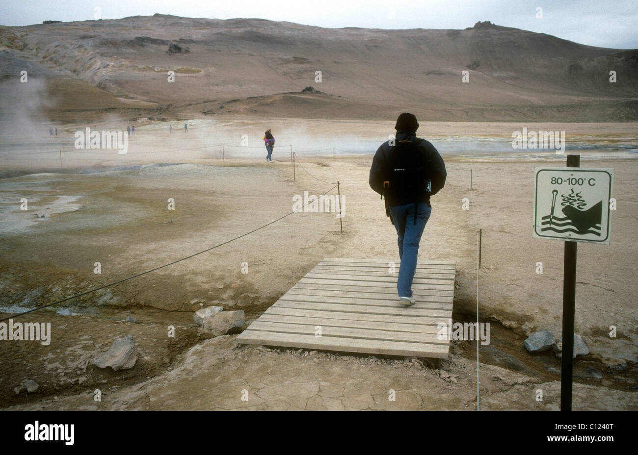 A tourist on a boardwalk passes a sign warning of very hot ground at ...
