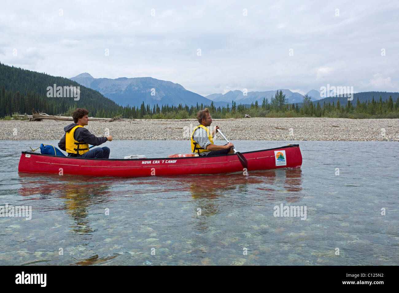Two men in a canoe, canoeing upper Liard River, clear, shallow water ...