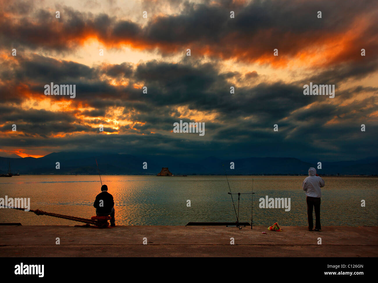 People fishing on the promenade of Nafplio town around sunset. Between ...