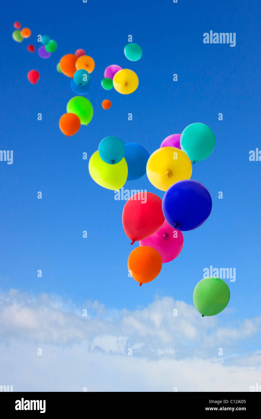 summers day with a host of coloured balloons floating into the blue sky ...