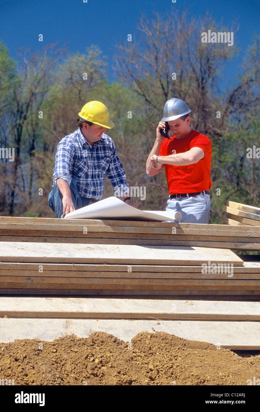 Two construction workers inspect architectural drawings at a commercial ...