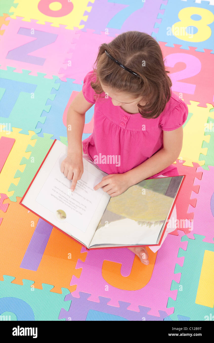 Young girl reading book on colorful floor mat Stock Photo - Alamy