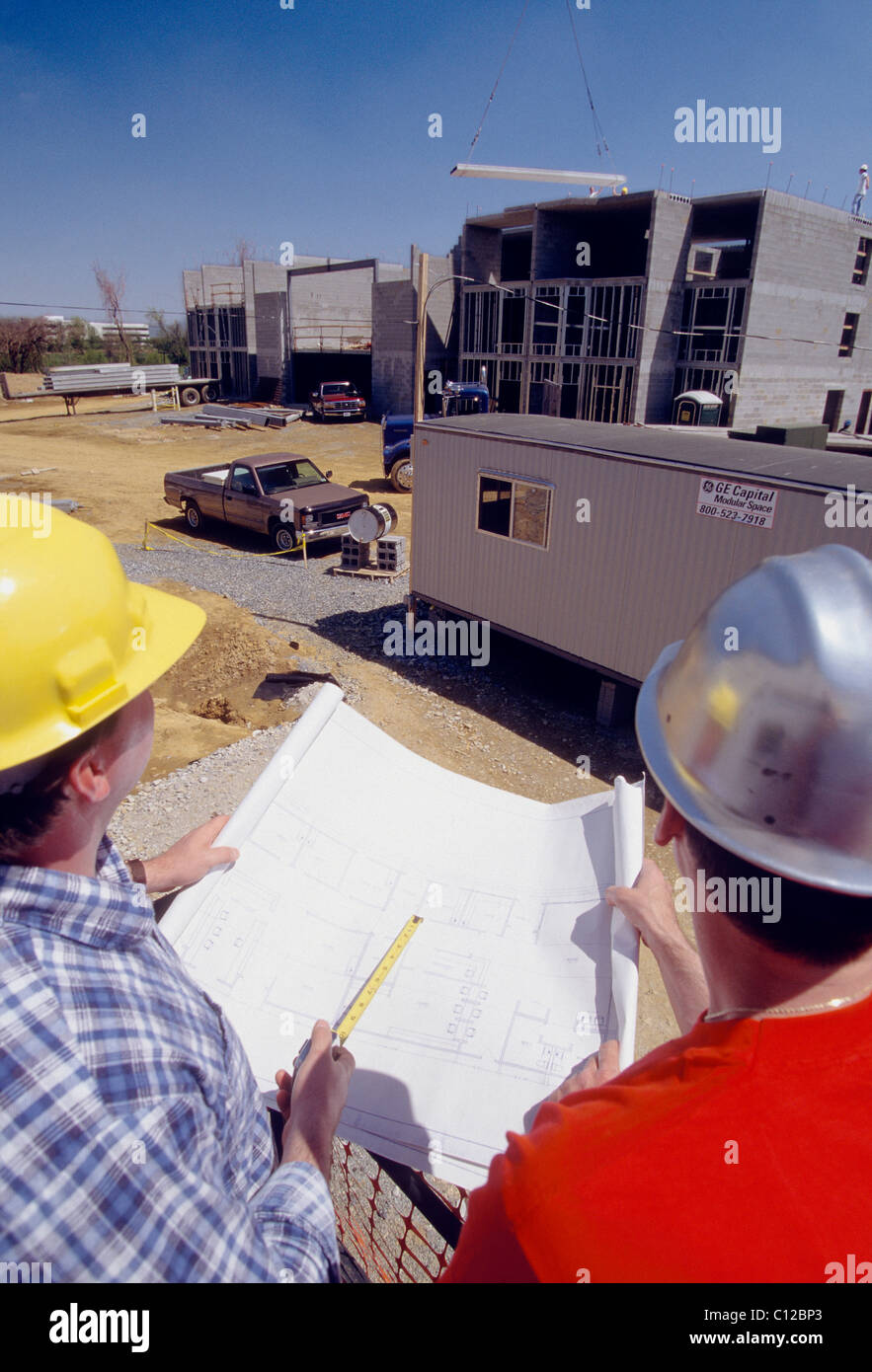 Two construction workers inspect architectural drawings at a commercial ...