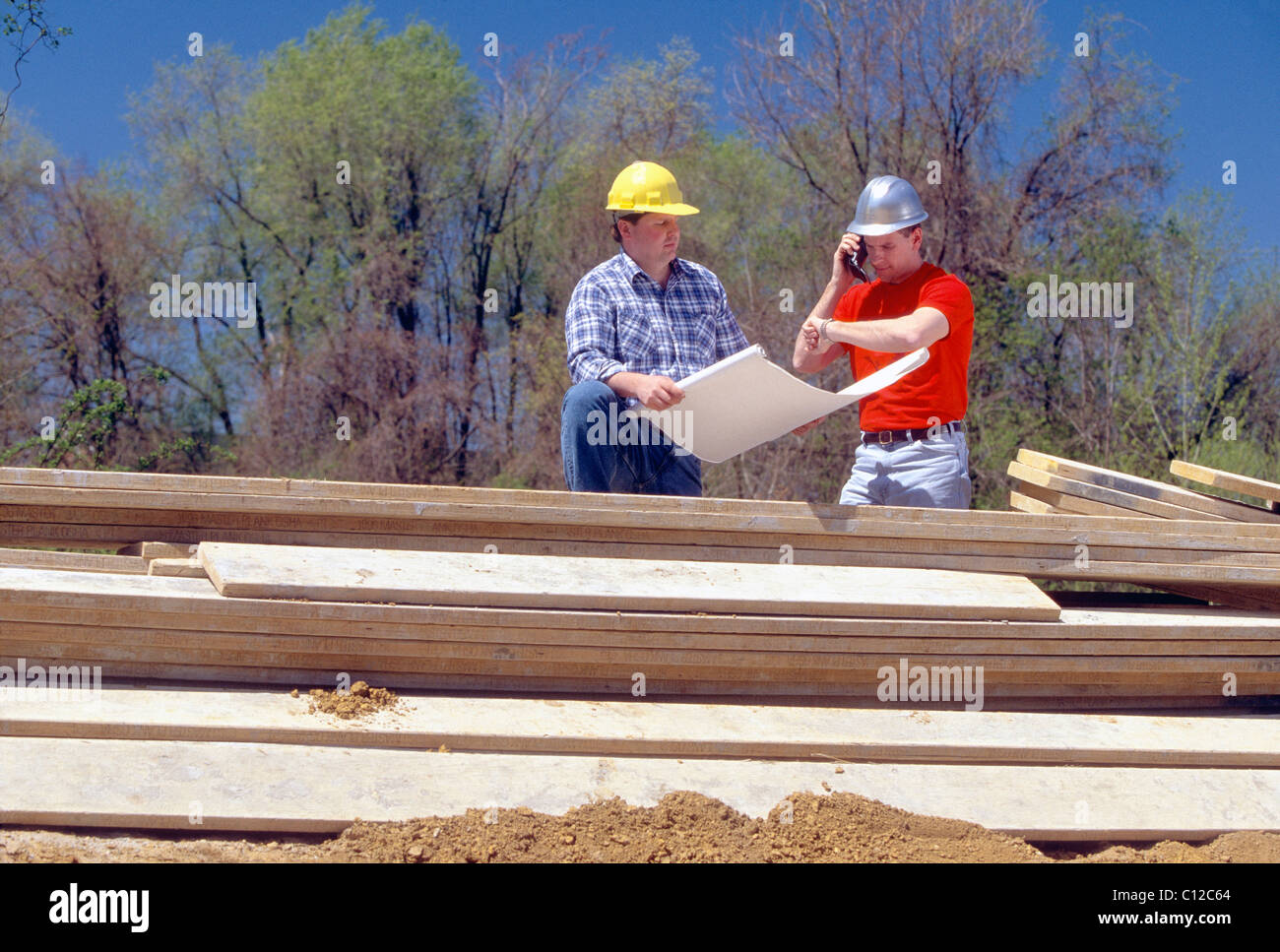 Two construction workers inspect architectural drawings at a commercial ...