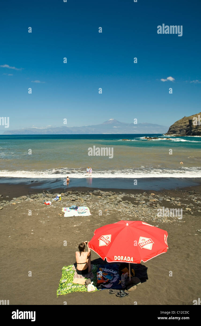 La Gomera, Canary Islands. Sunbathing at Playa de La Caleta. Snow topped Pico del Teide ...
