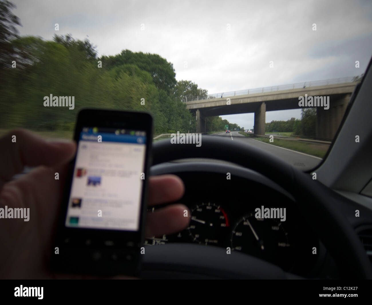 A Car driver driving whilst using a mobile device / mobile phone ...
