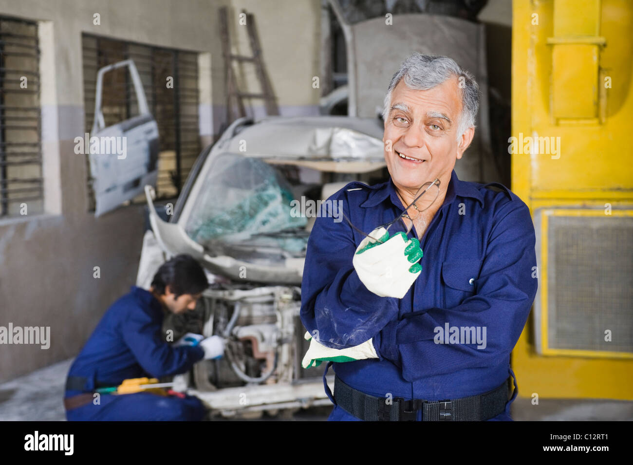 Portrait of an auto mechanic smiling with an apprentice repairing a car ...