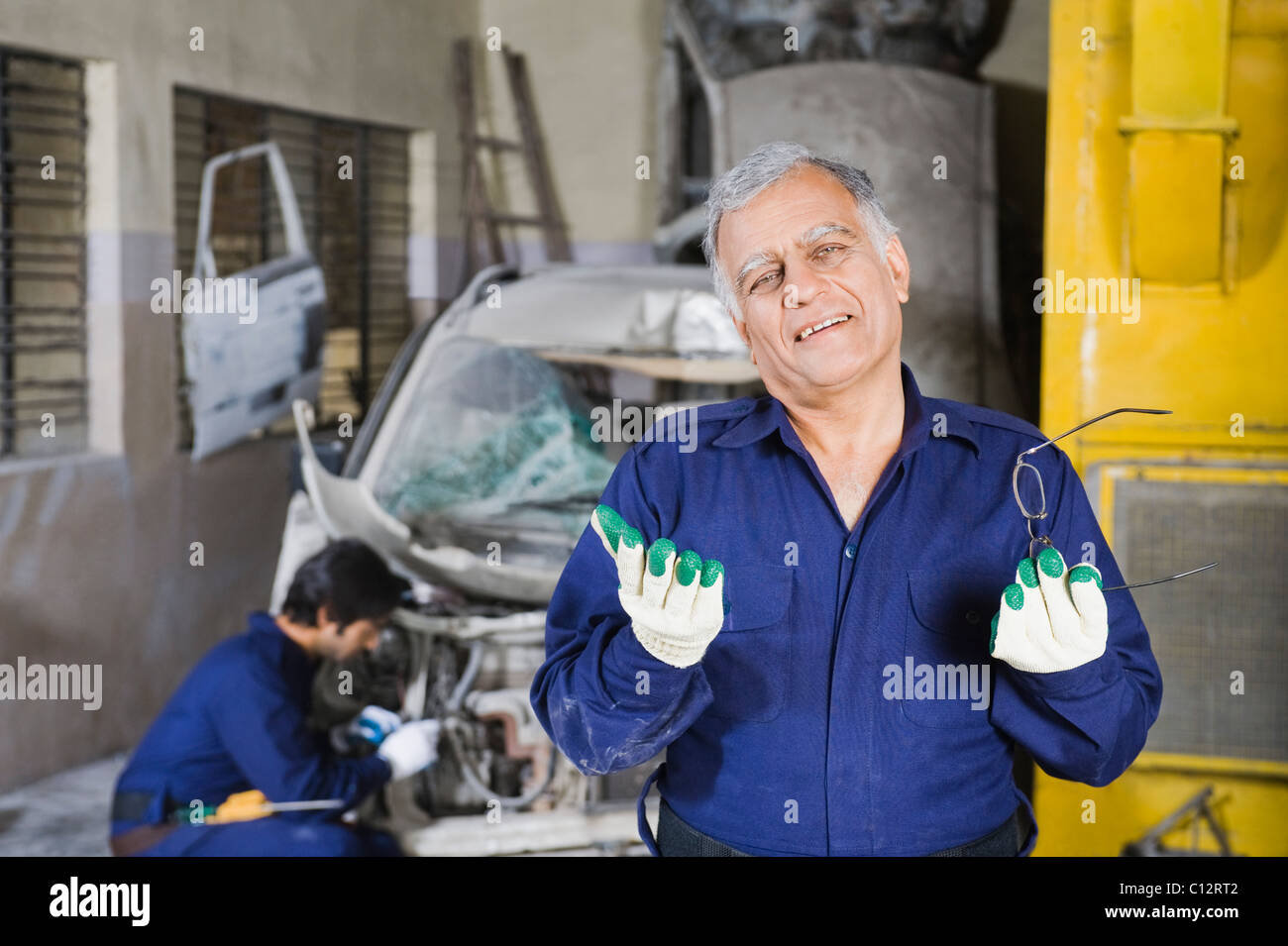 Portrait of an auto mechanic gesturing with an apprentice repairing a ...
