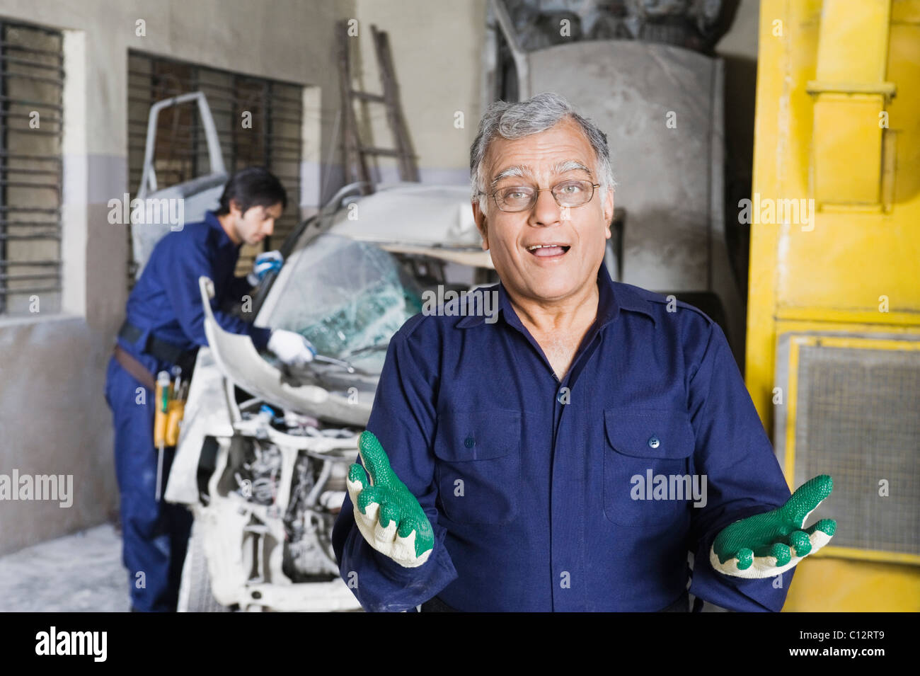 Portrait of an auto mechanic gesturing with an apprentice repairing a ...