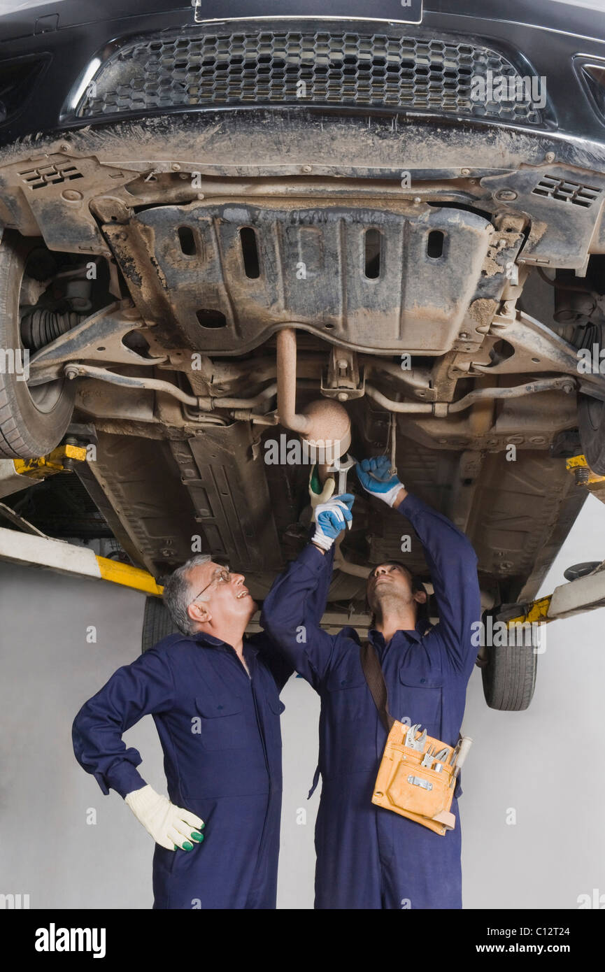 Auto mechanic with an apprentice working under a raised car in a garage ...