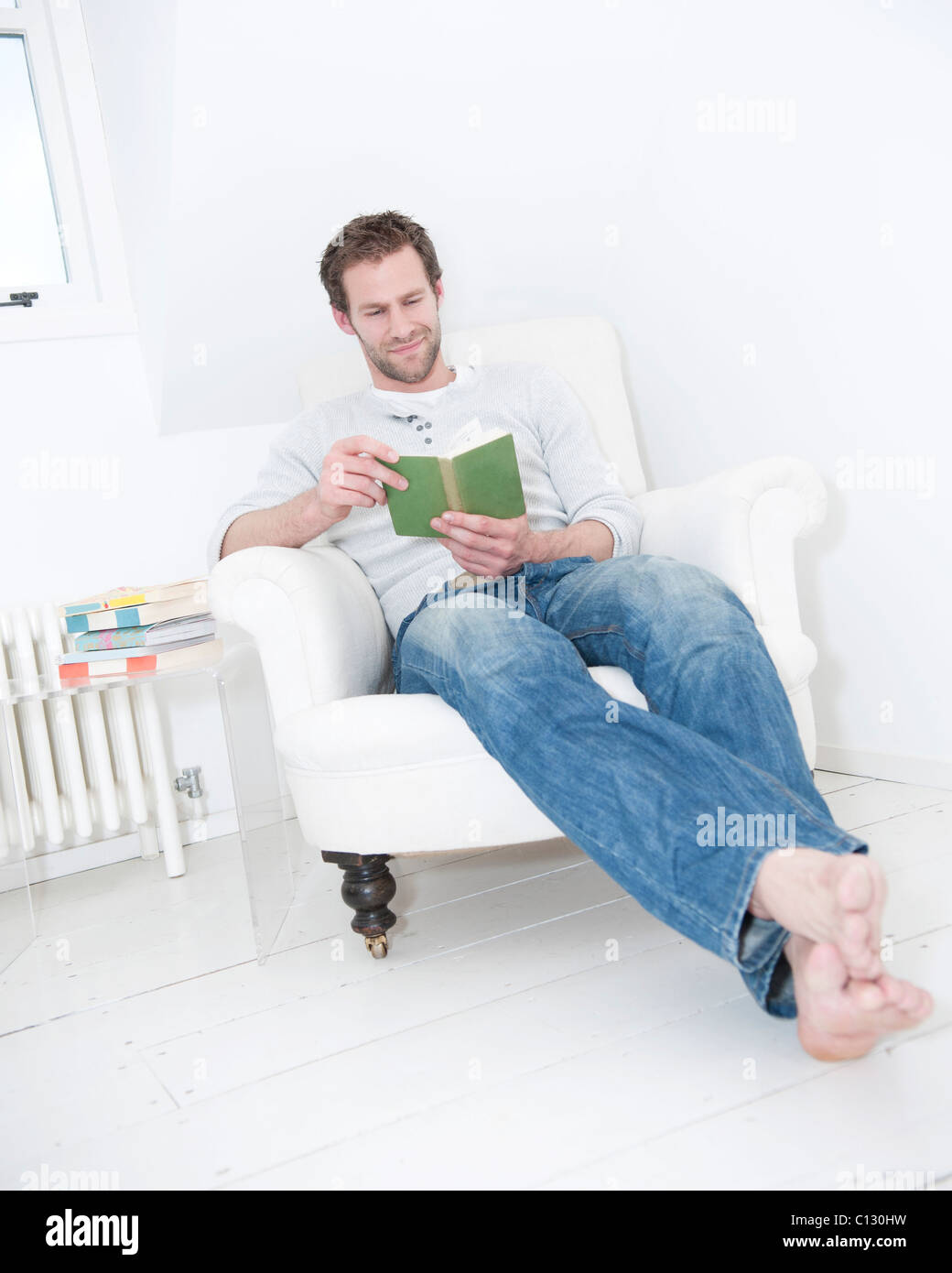 young man sitting in arm chair reading book Stock Photo - Alamy