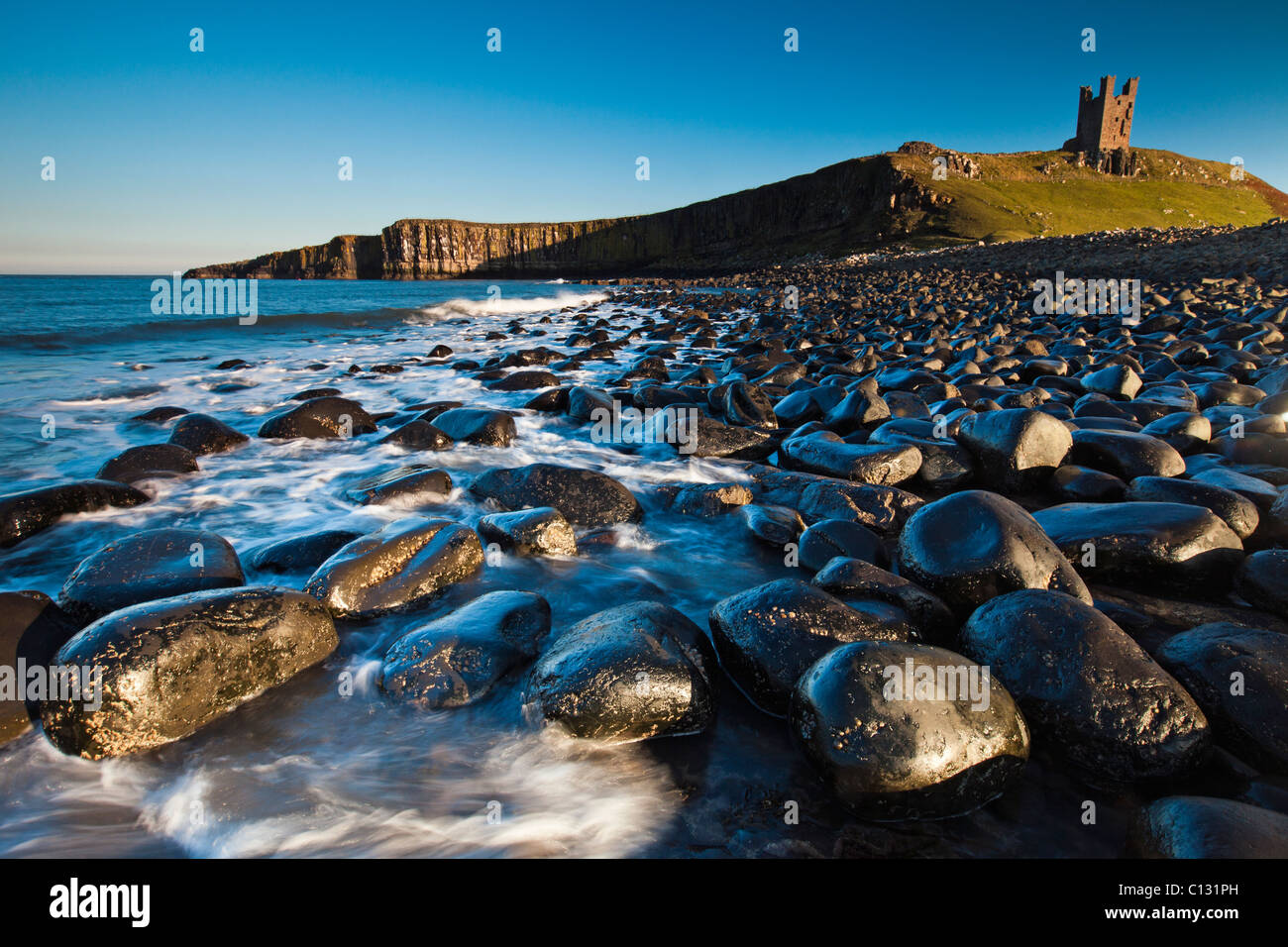 Dunstanburgh Castle, with basalt boulders on beach, autumn ...