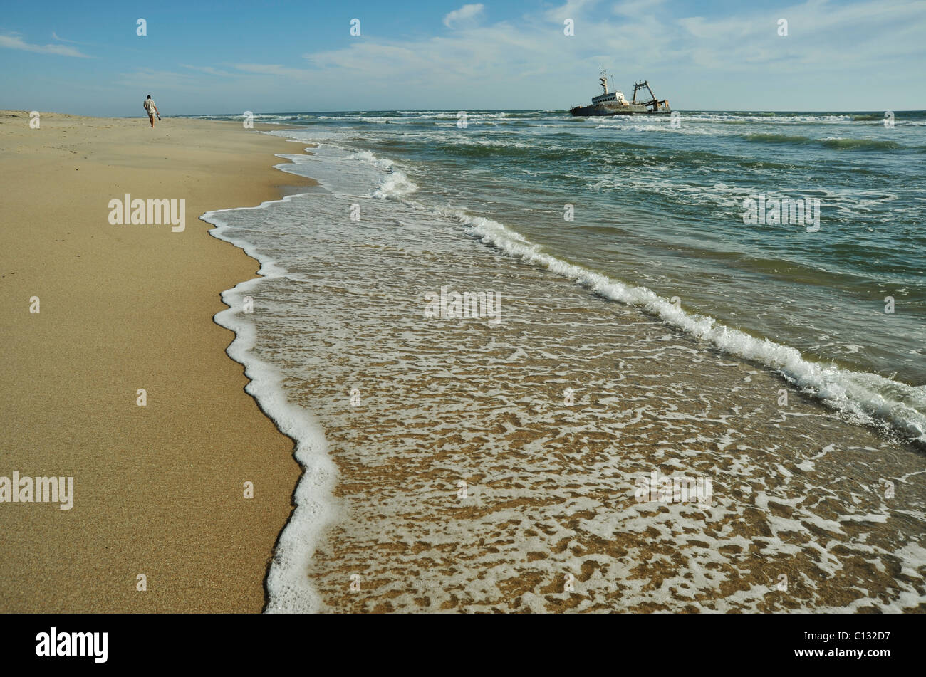 Seascape of lone man walking on desolate beach with ship wreck in ...
