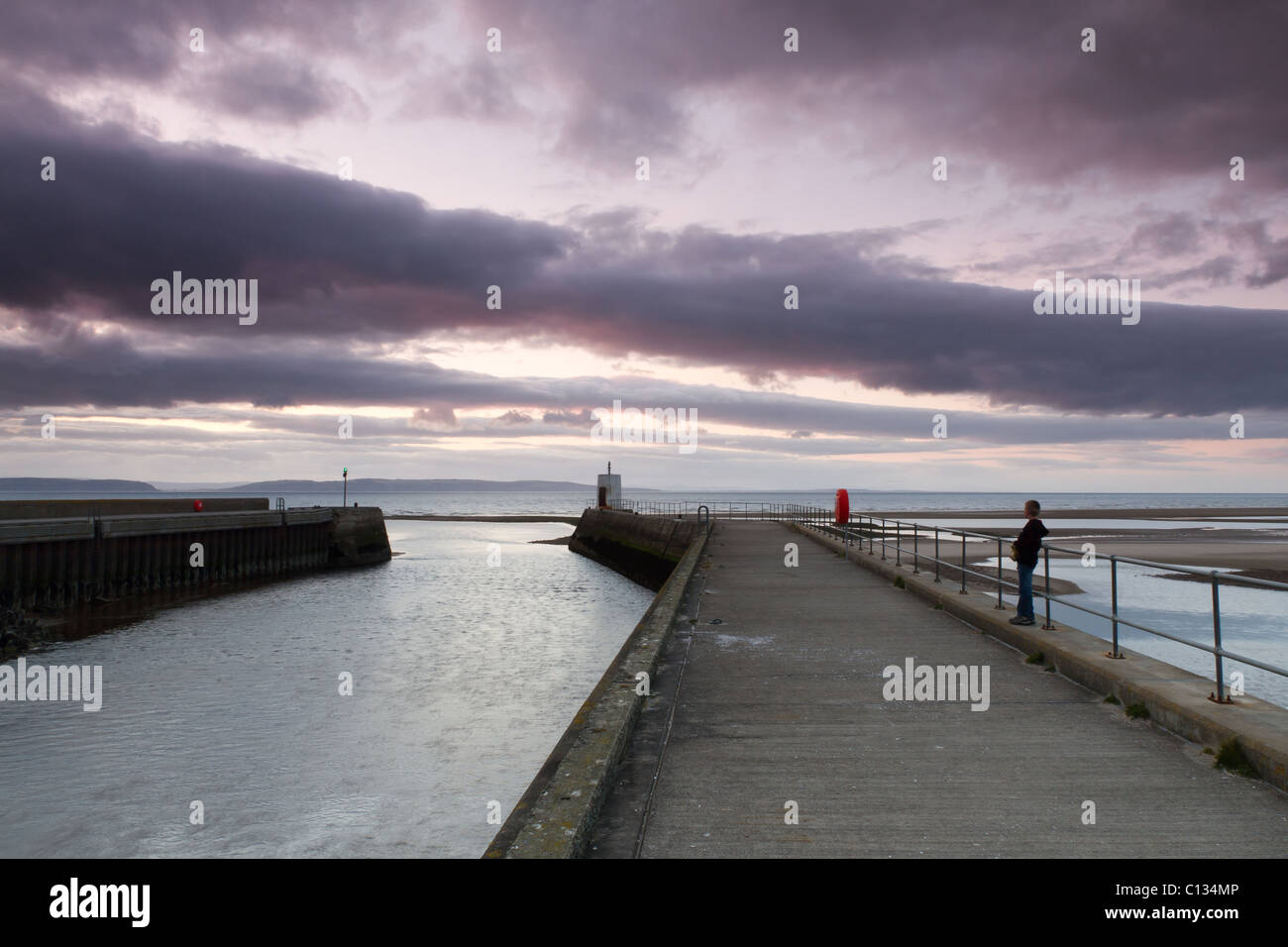 A boy standing on a dock, looking out to sea at sunset Stock Photo - Alamy