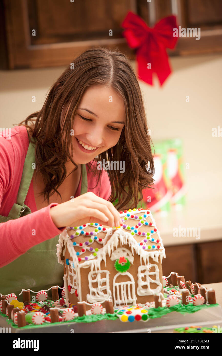 USA, Utah, Lehi, Young woman decorating gingerbread house in kitchen ...