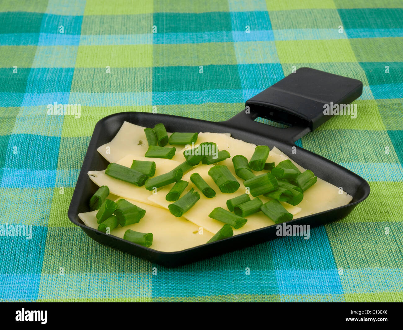 Raclette pan with edam cheese and spring onion on colorful tablecloth ...