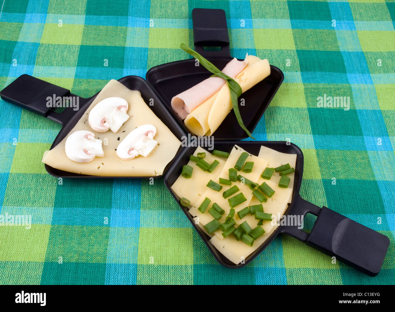 Three raclette pans with cheese, spring onion, mushrooms and ham on ...
