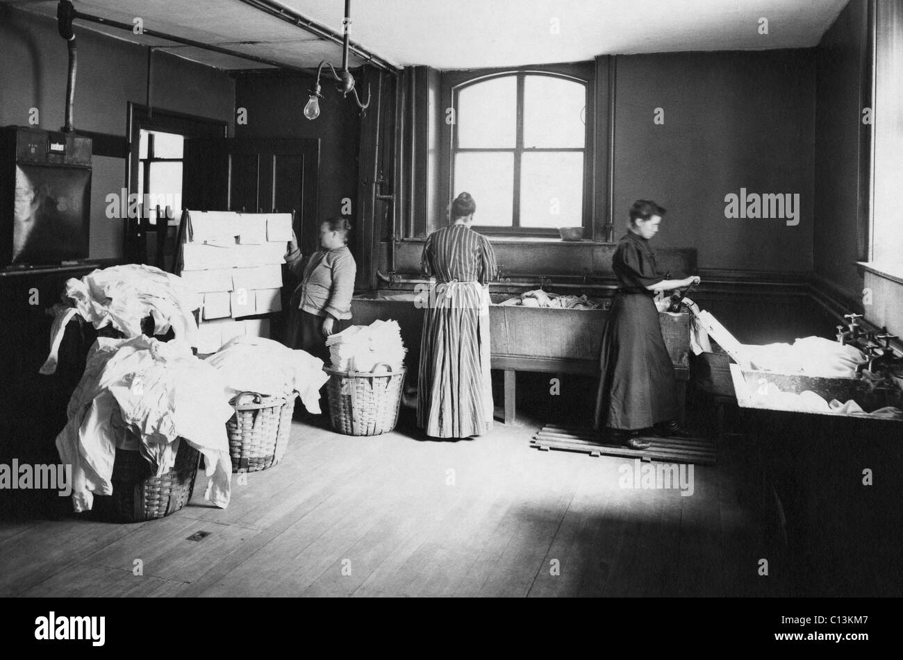 Laundry with women working at large sinks, one operating a hand cranked ...