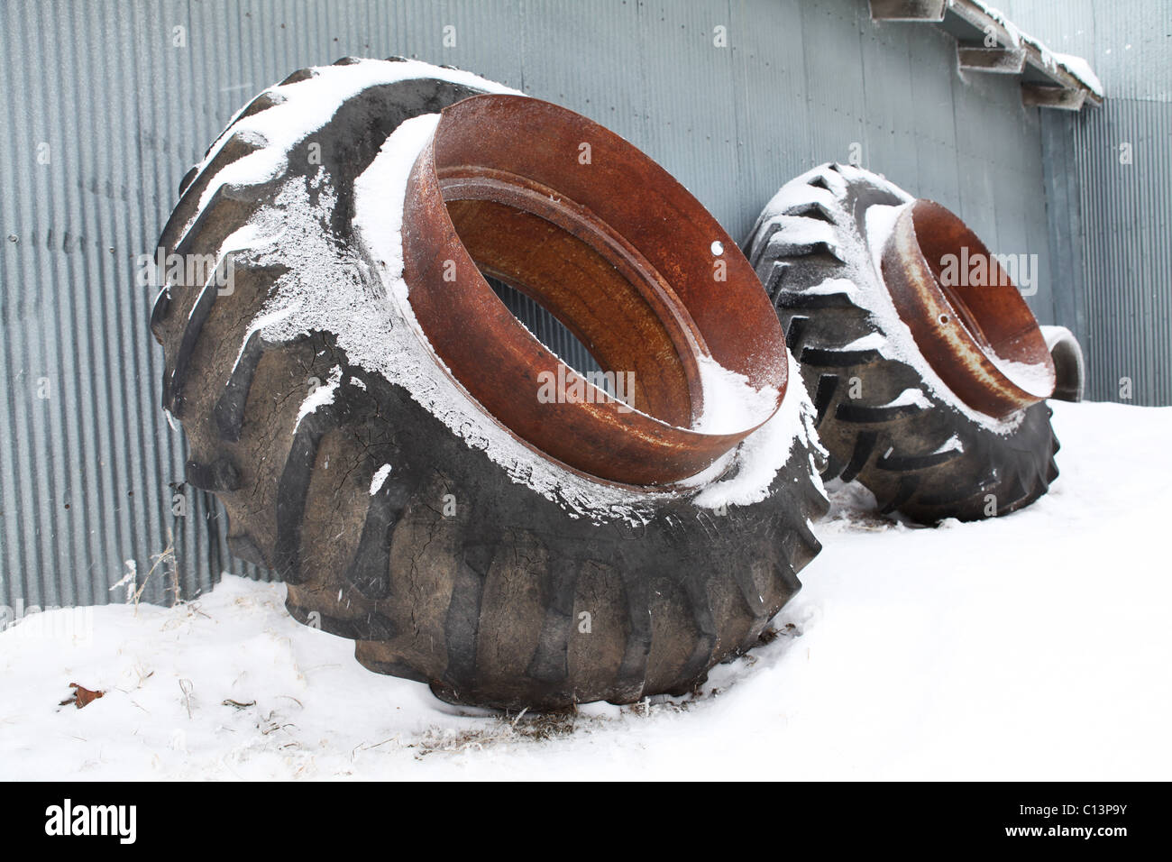 Large tractor tires with rim leaning on tin shed in snow Stock Photo ...