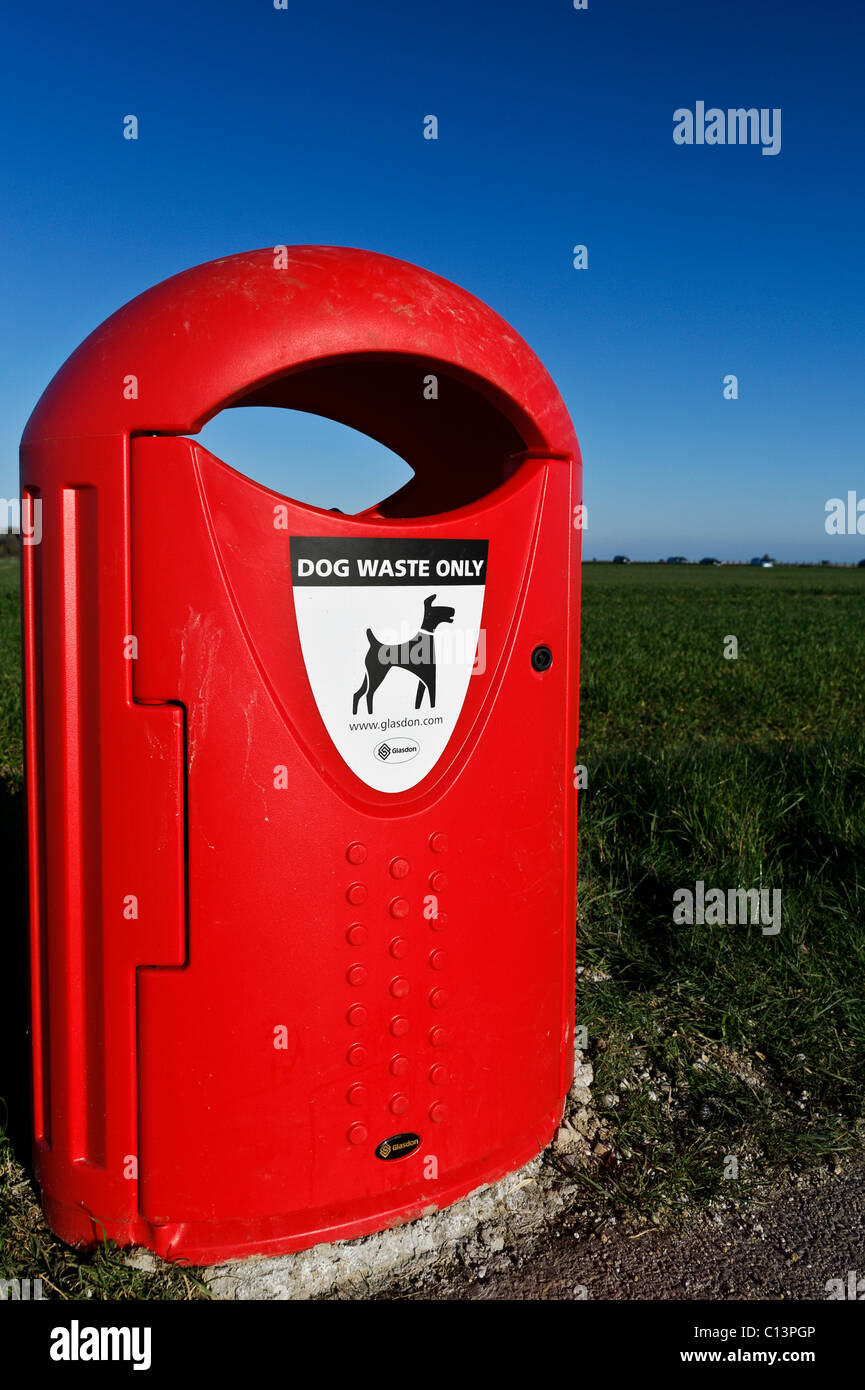 A bright red Dog Waste Bin next to a green field with a very blue sky ...